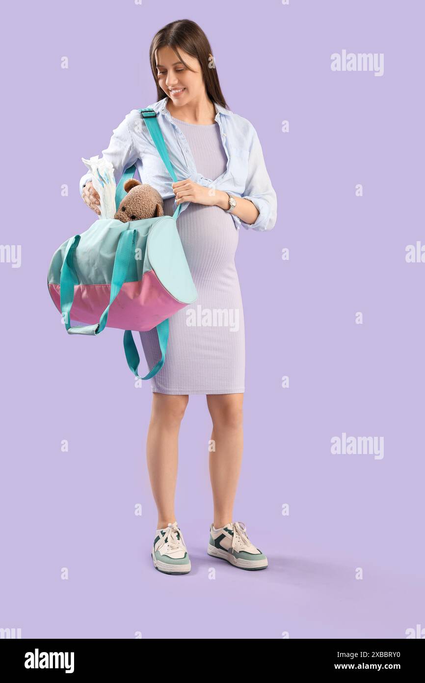 Young pregnant woman with diapers and maternity hospital bag on lilac ...