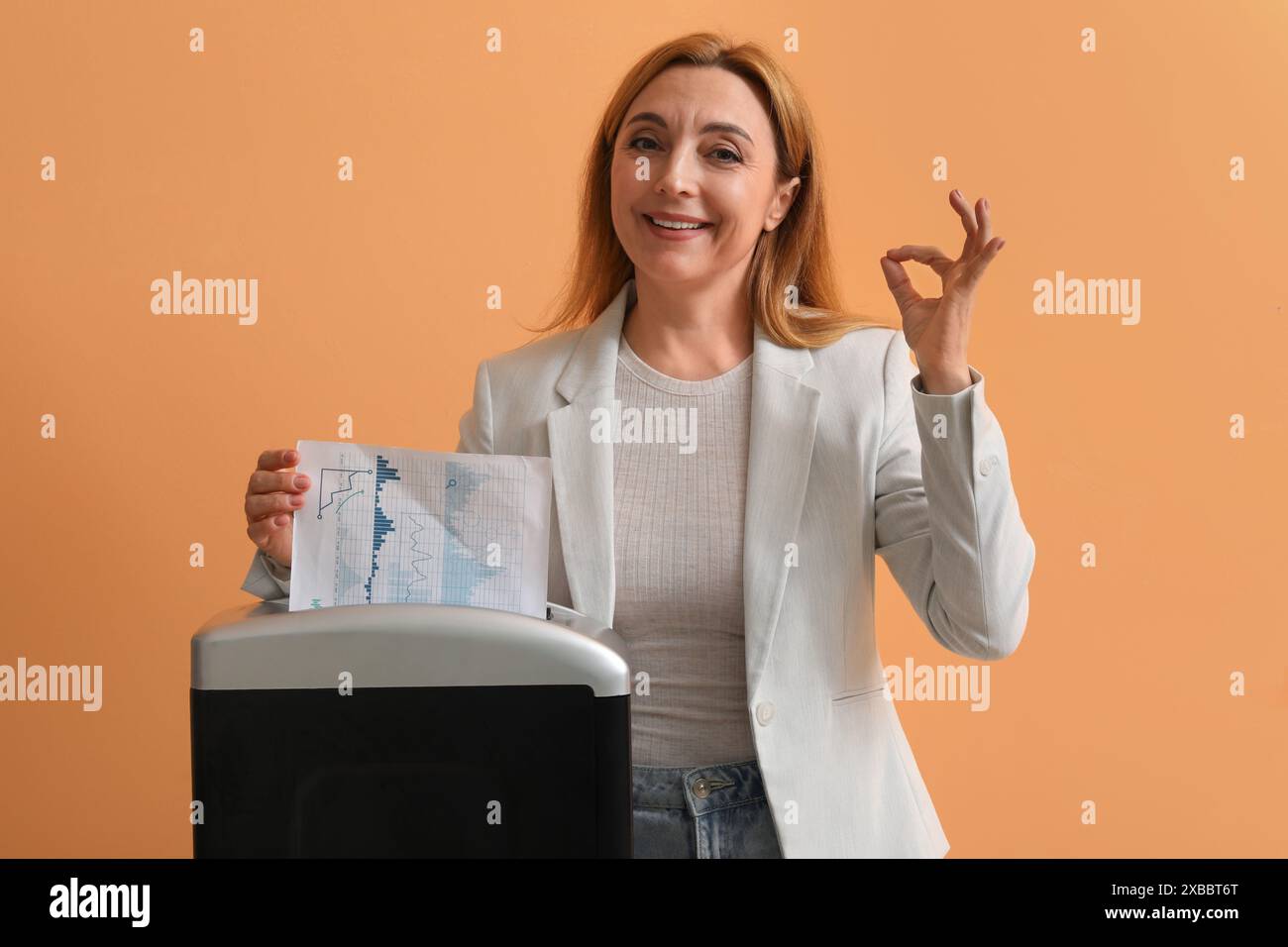 Adult woman destroying documents using shredder and showing OK gesture ...
