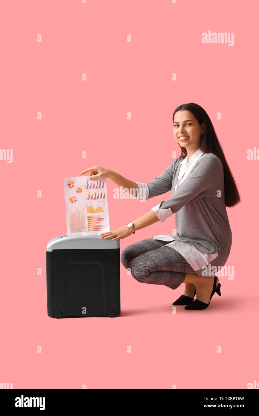 Young woman destroying documents using shredder on pink background ...