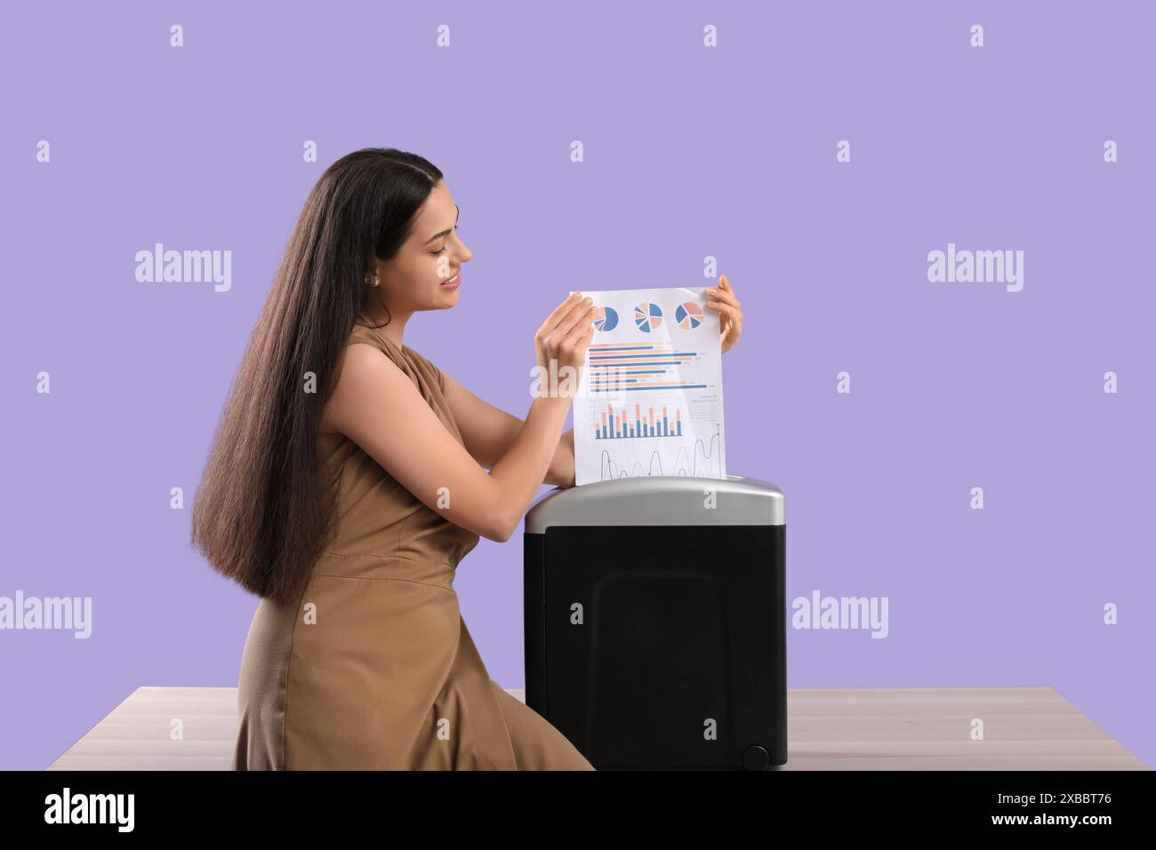 Young woman destroying documents using shredder on table against lilac ...