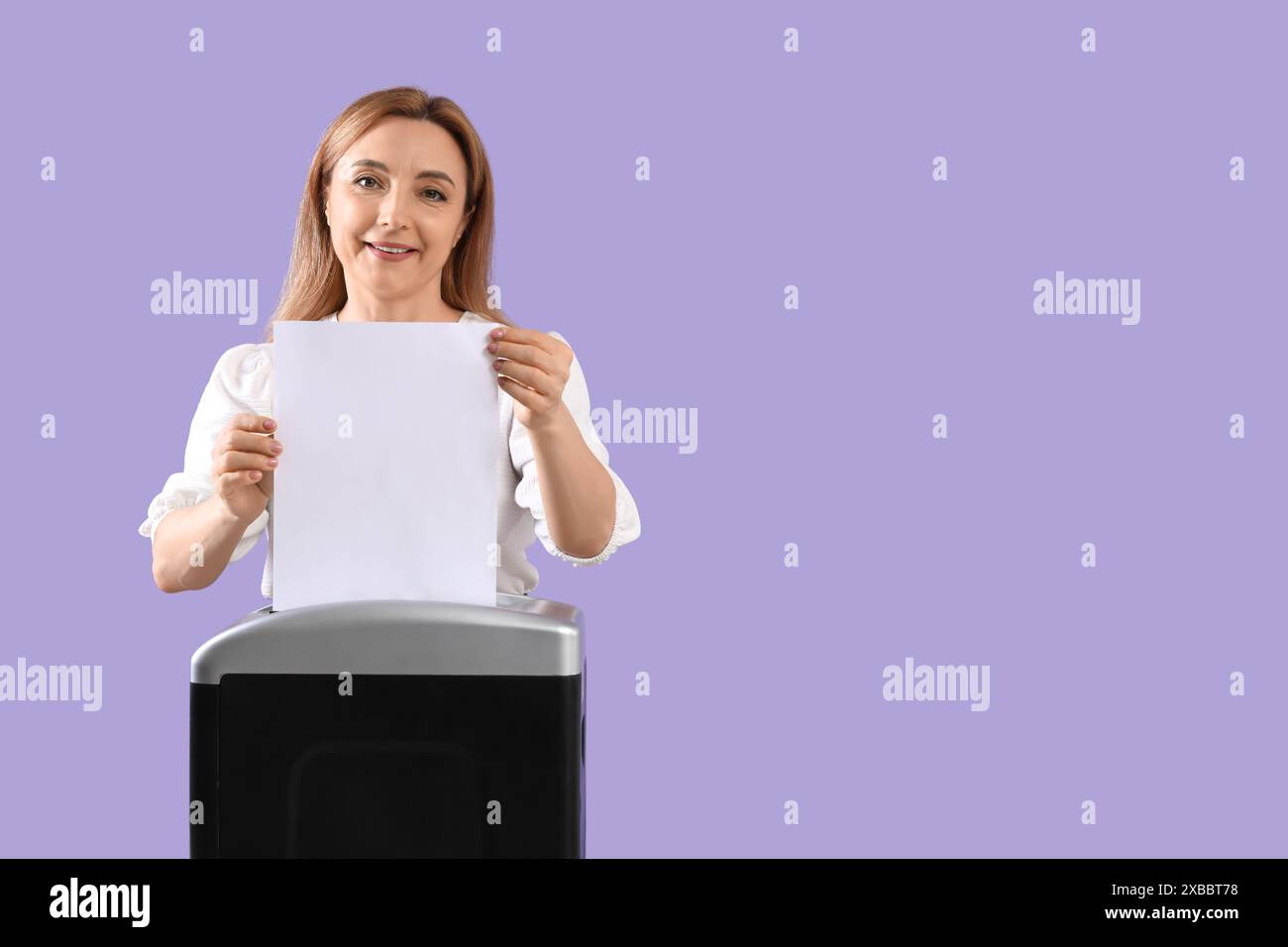 Adult woman destroying paper sheet using shredder on lilac background ...