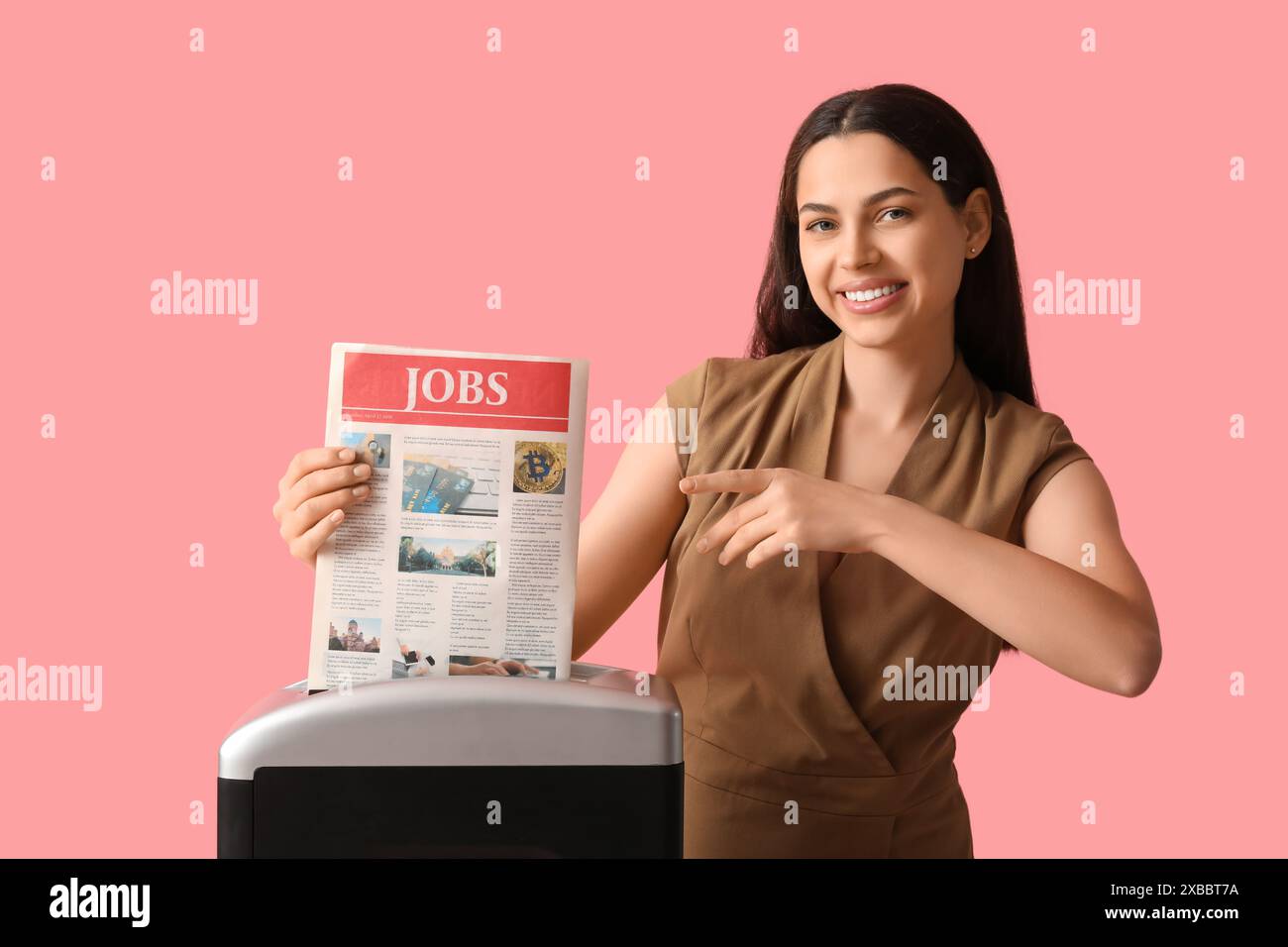 Happy young woman pointing at newspaper and shredder on pink background ...