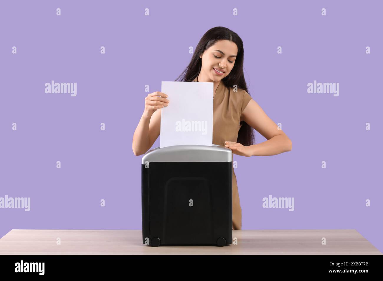Young woman destroying paper sheet using shredder on table against ...