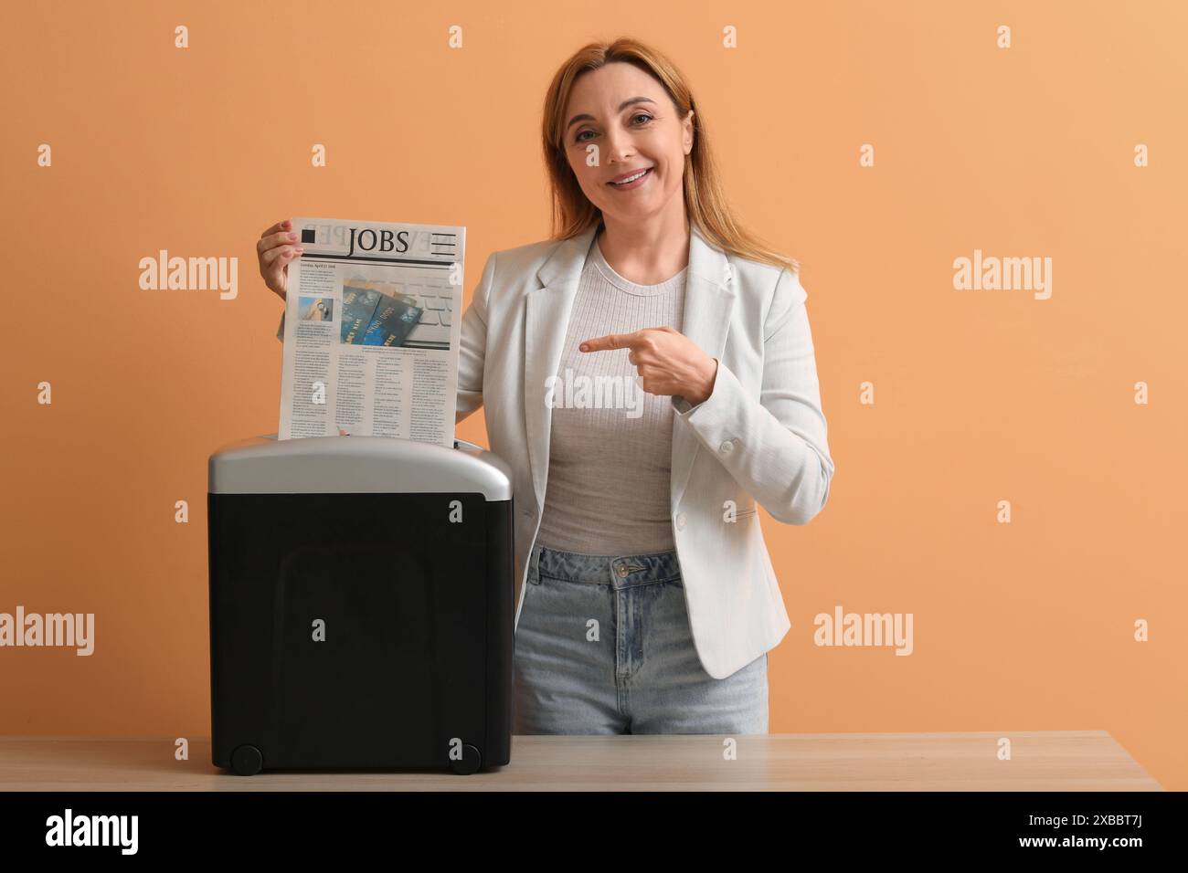 Adult woman pointing at newspaper and shredder on orange background ...