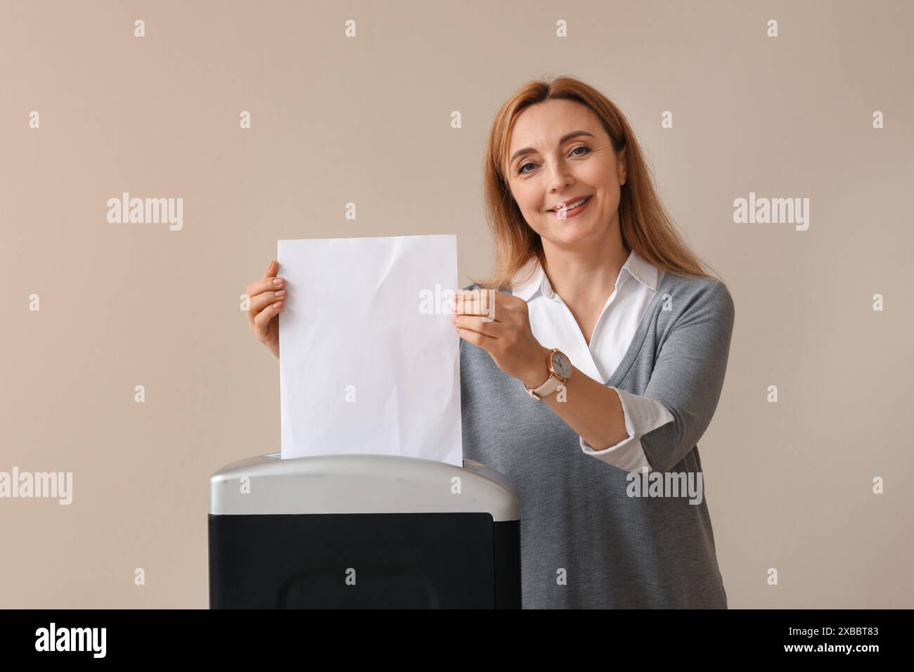 Adult woman destroying paper sheet using shredder on light background ...