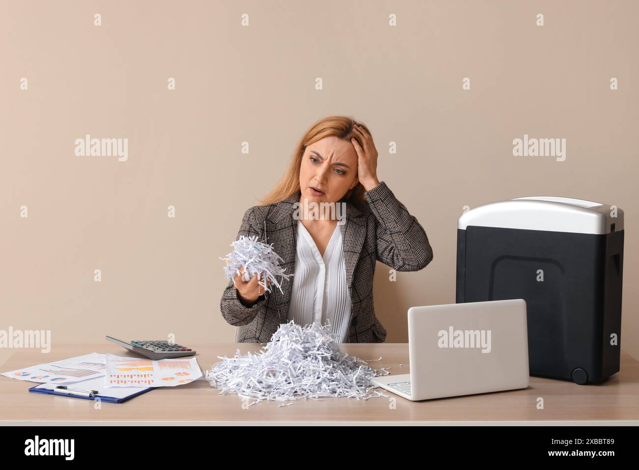 Shocked adult secretary with shredded paper, shredder and laptop ...