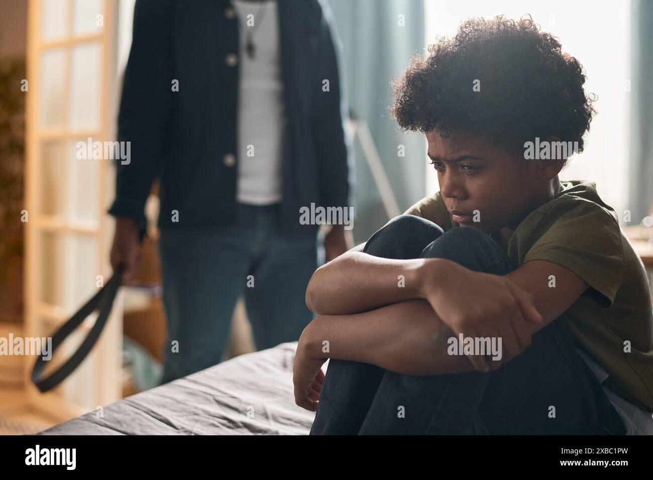 Side view portrait of Black little boy crying sitting on bed in dark ...