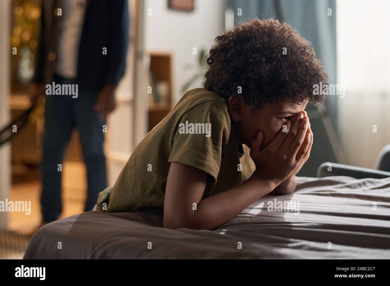 Side view portrait of crying African American boy hiding in his room ...