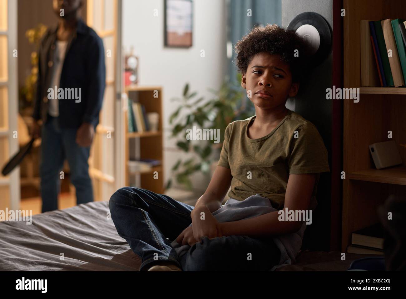 Father and son fight with focus on upset young boy sitting on bed and ...