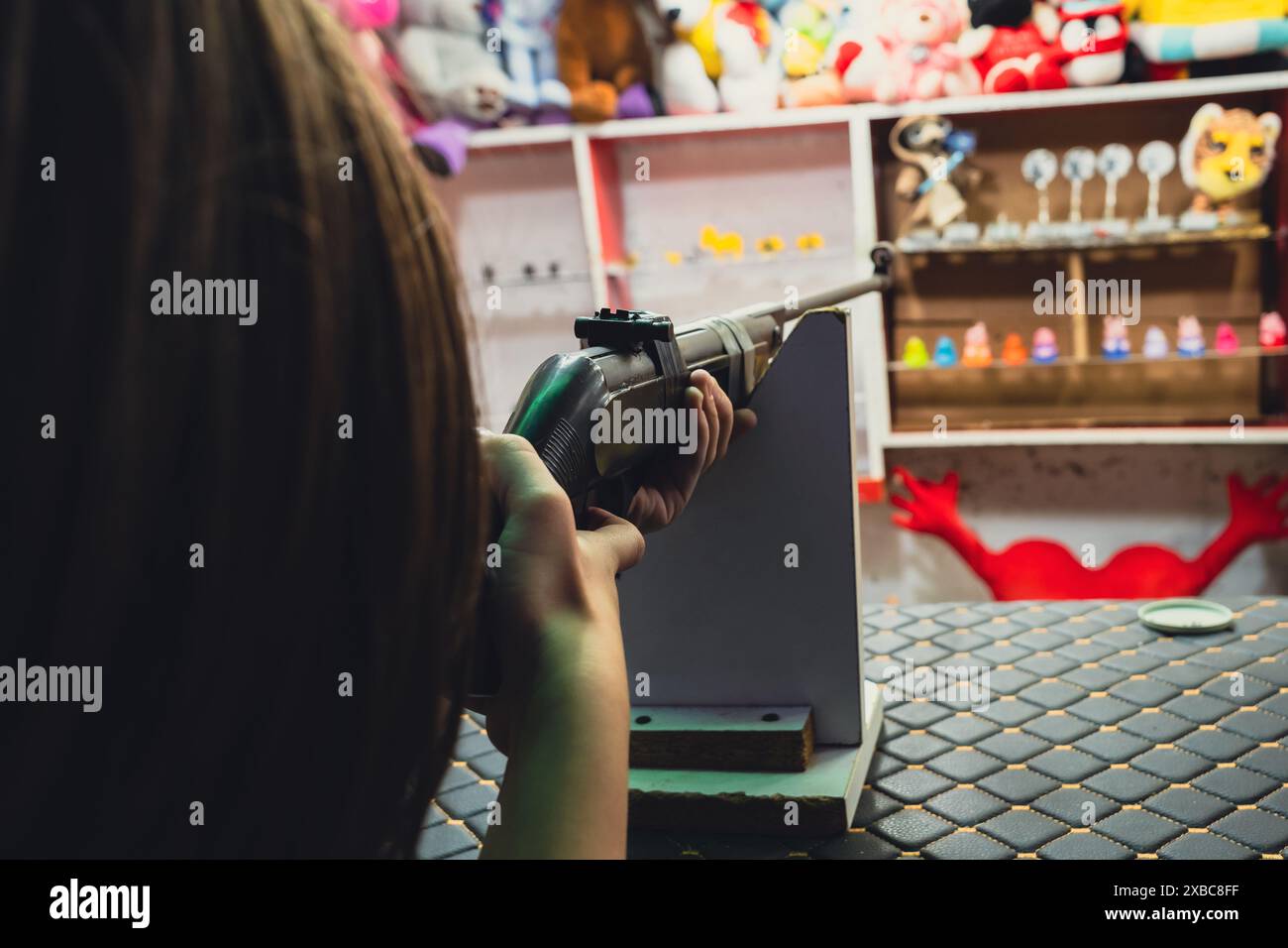 A young girl aiming a rifle at a target in a shooting game booth filled ...