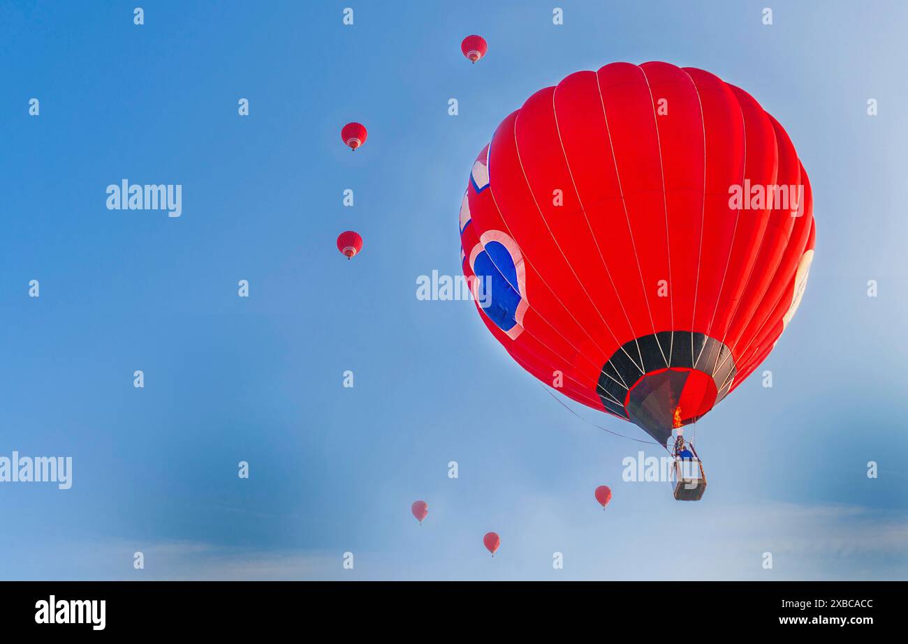 Red hot air balloon floating in the blue sky with smaller balloons in ...
