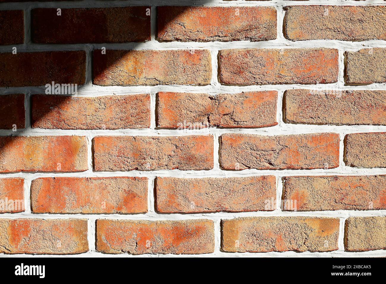 Sunlight and shadow on a textured red brick wall with white mortar ...