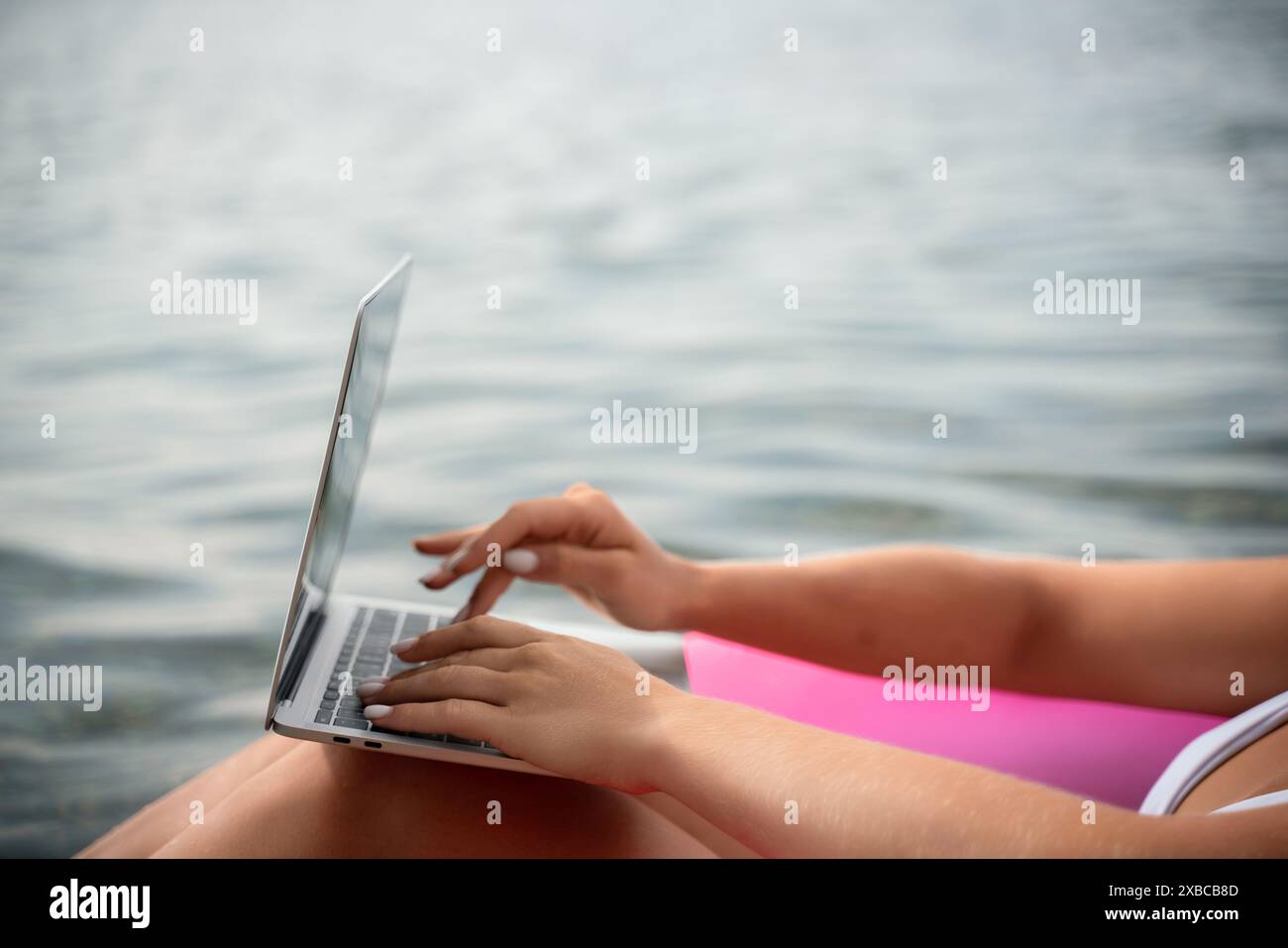 A woman is sitting in a pink float on a lake, typing on a laptop ...