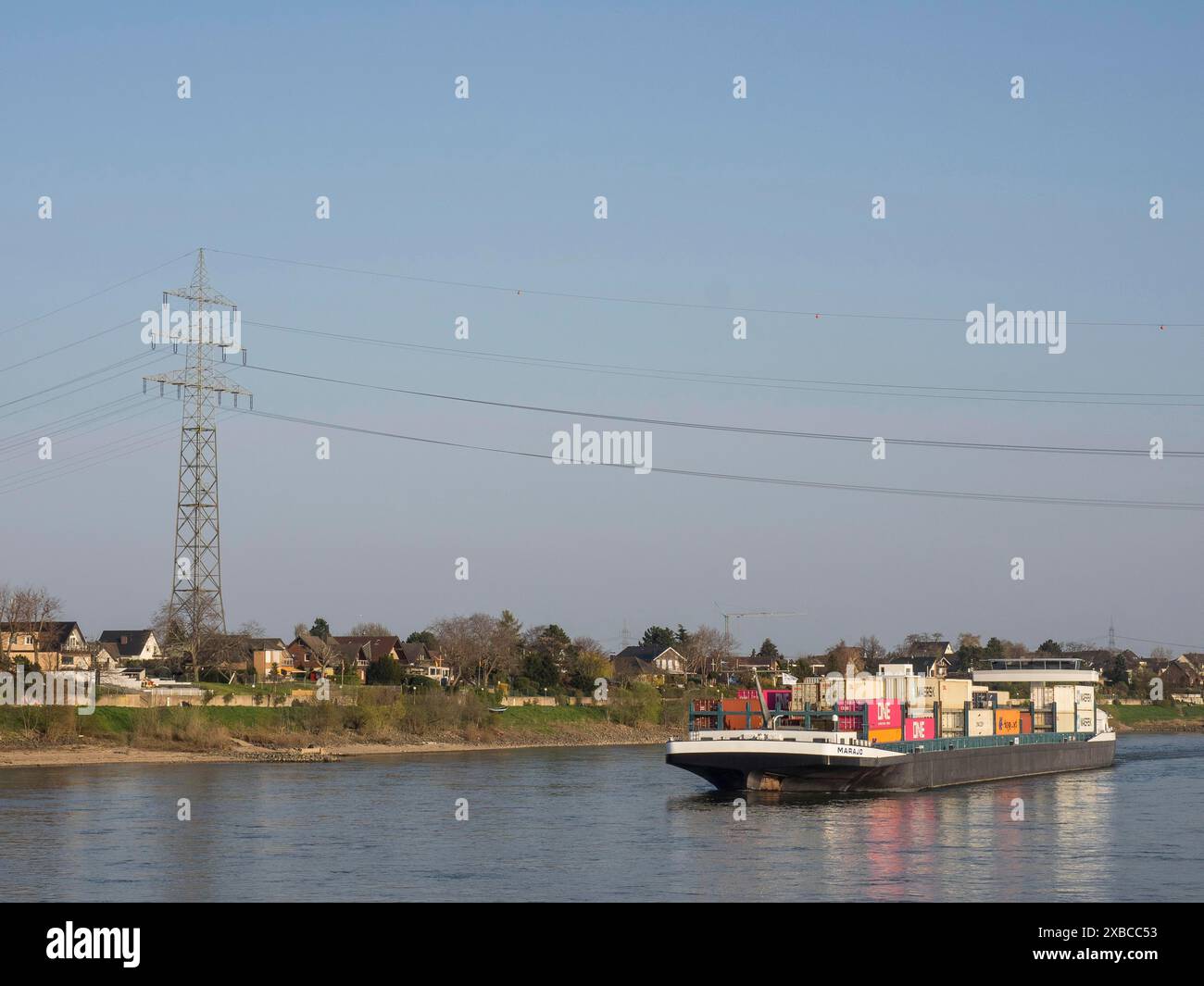A container ship sails on the river near a village with a high-voltage ...
