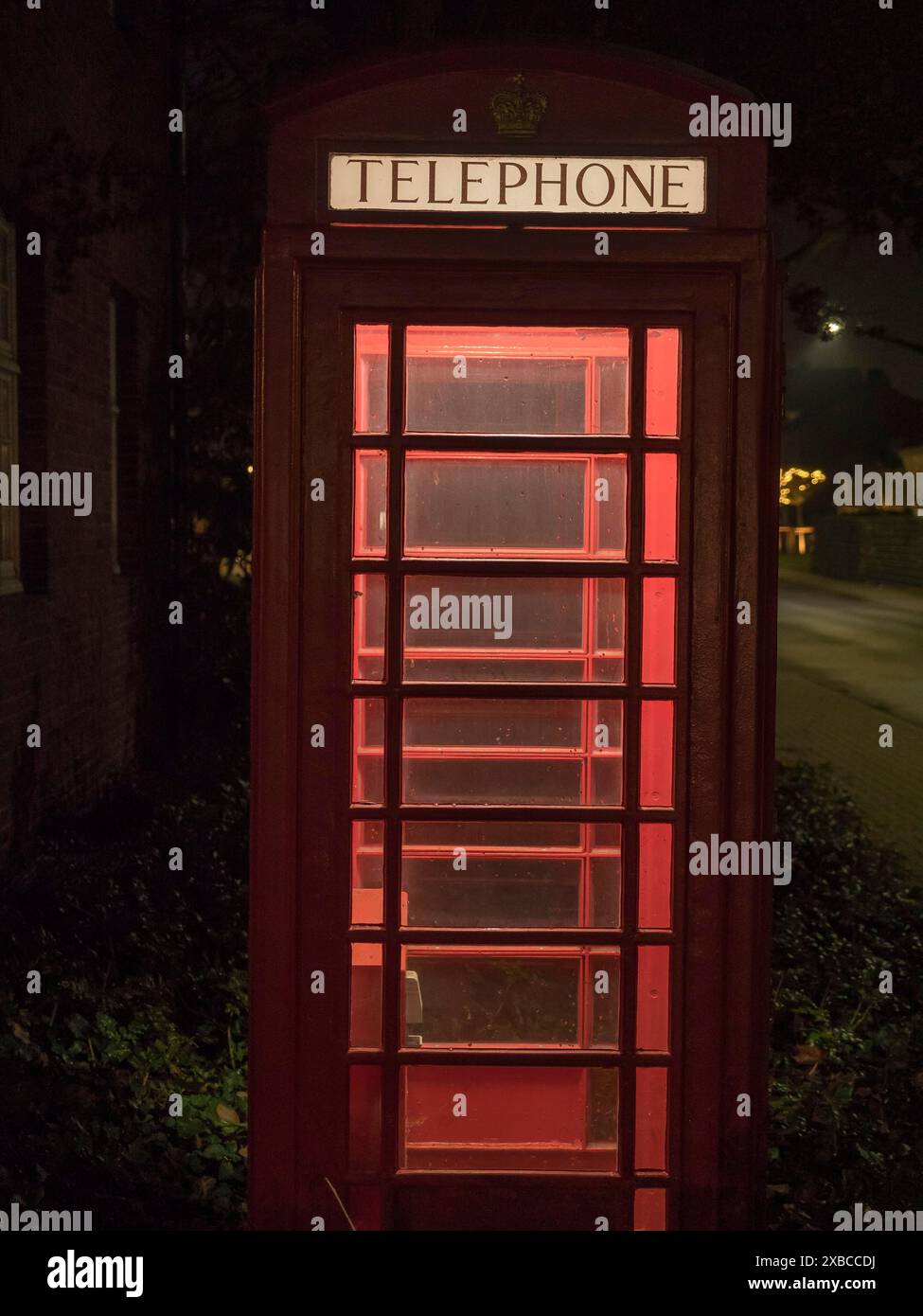 A red telephone box at night, illuminated from the inside and ...