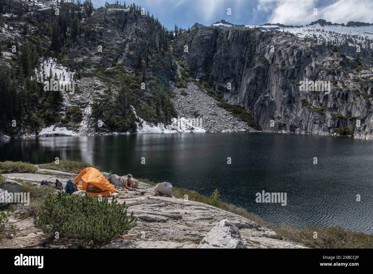 A campsite and tent at the edge of a mountain lake in the mountains of ...