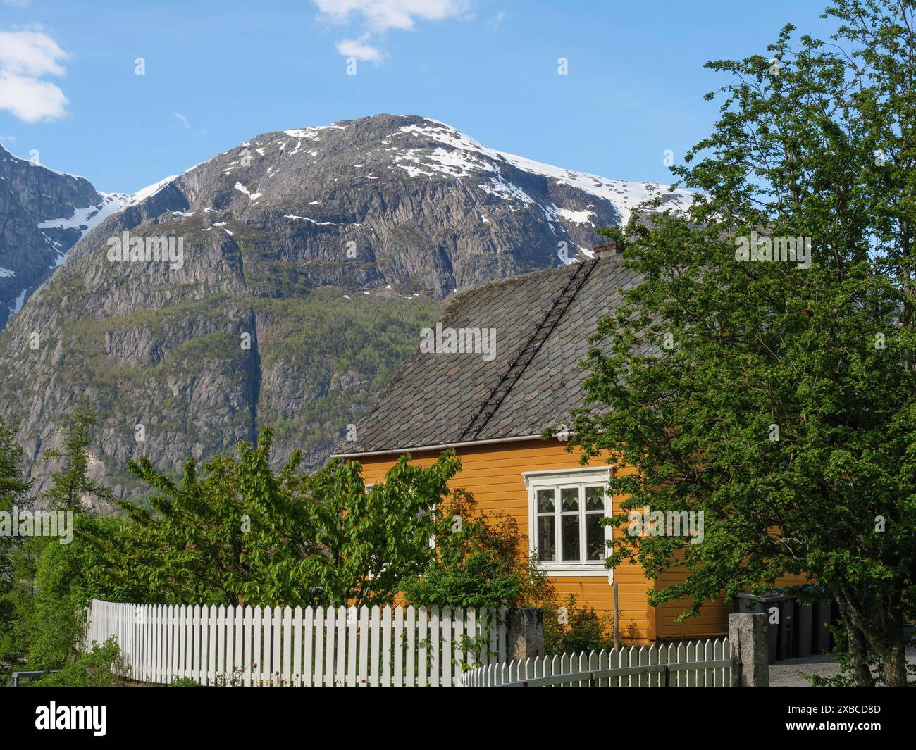 Cosy house with white fence and trees in a green village surrounded by ...