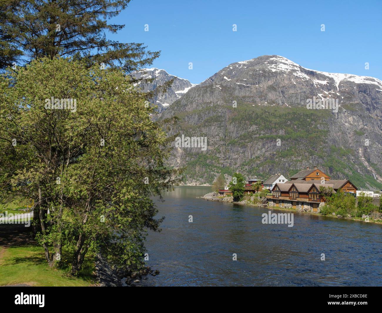 Calm river surrounded by houses, trees and mountains under a clear sky ...