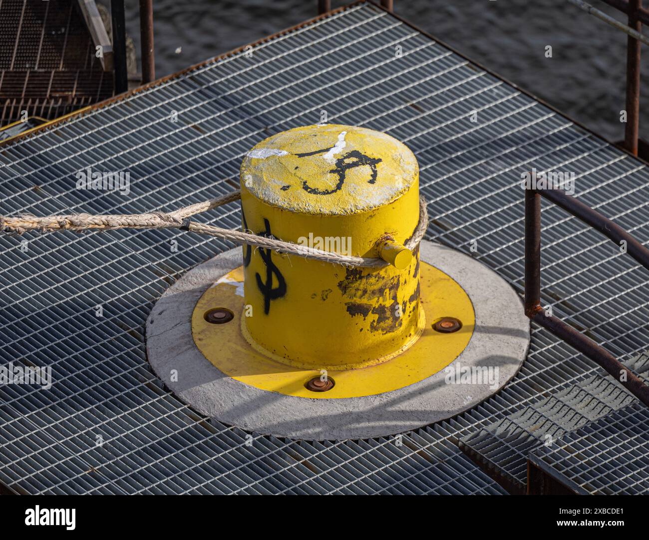 Close-up of a yellow bollard with a rope tied around it on a metal dock ...