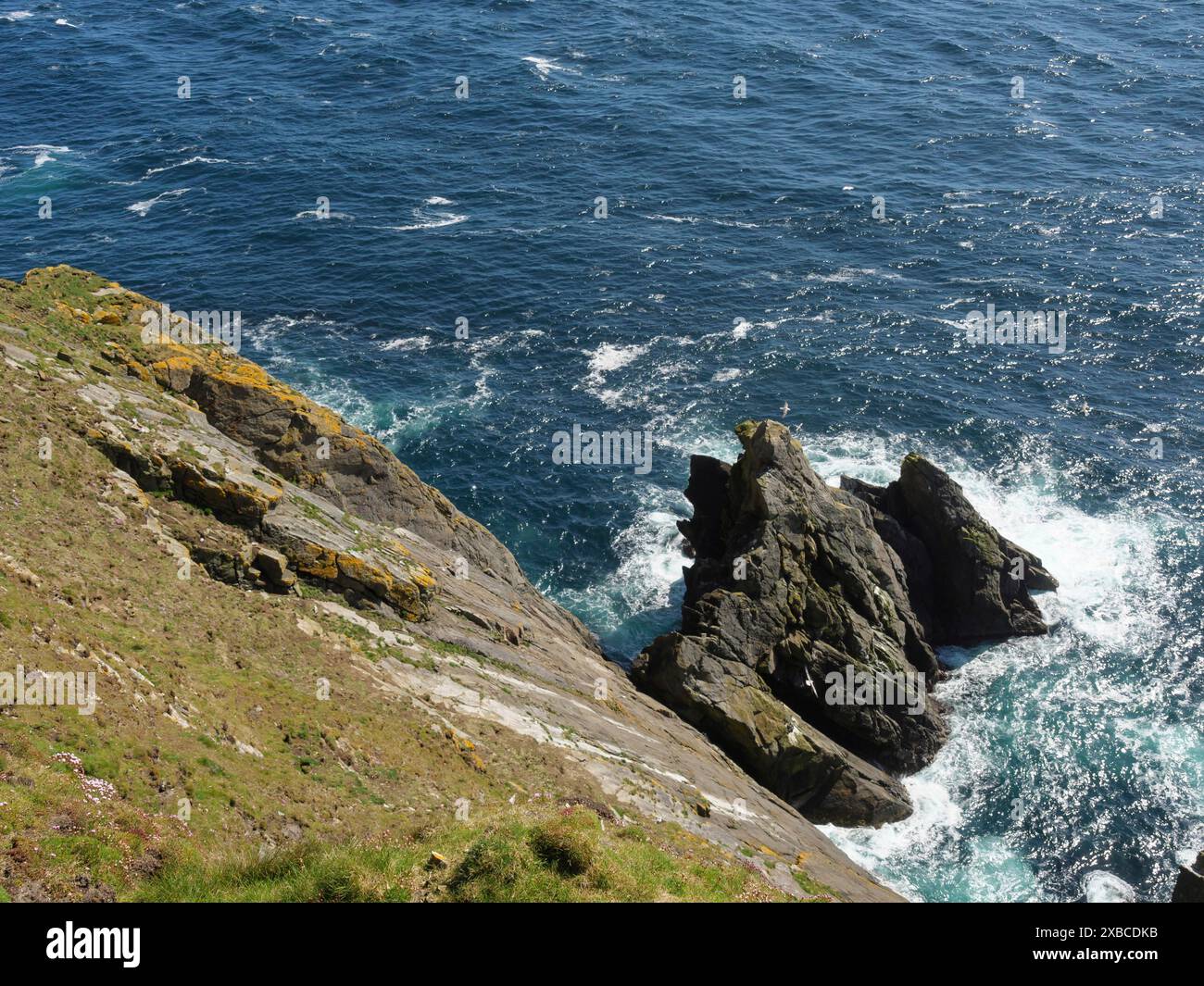 Steep cliffs meet turbulent blue seawater with white spray waves ...