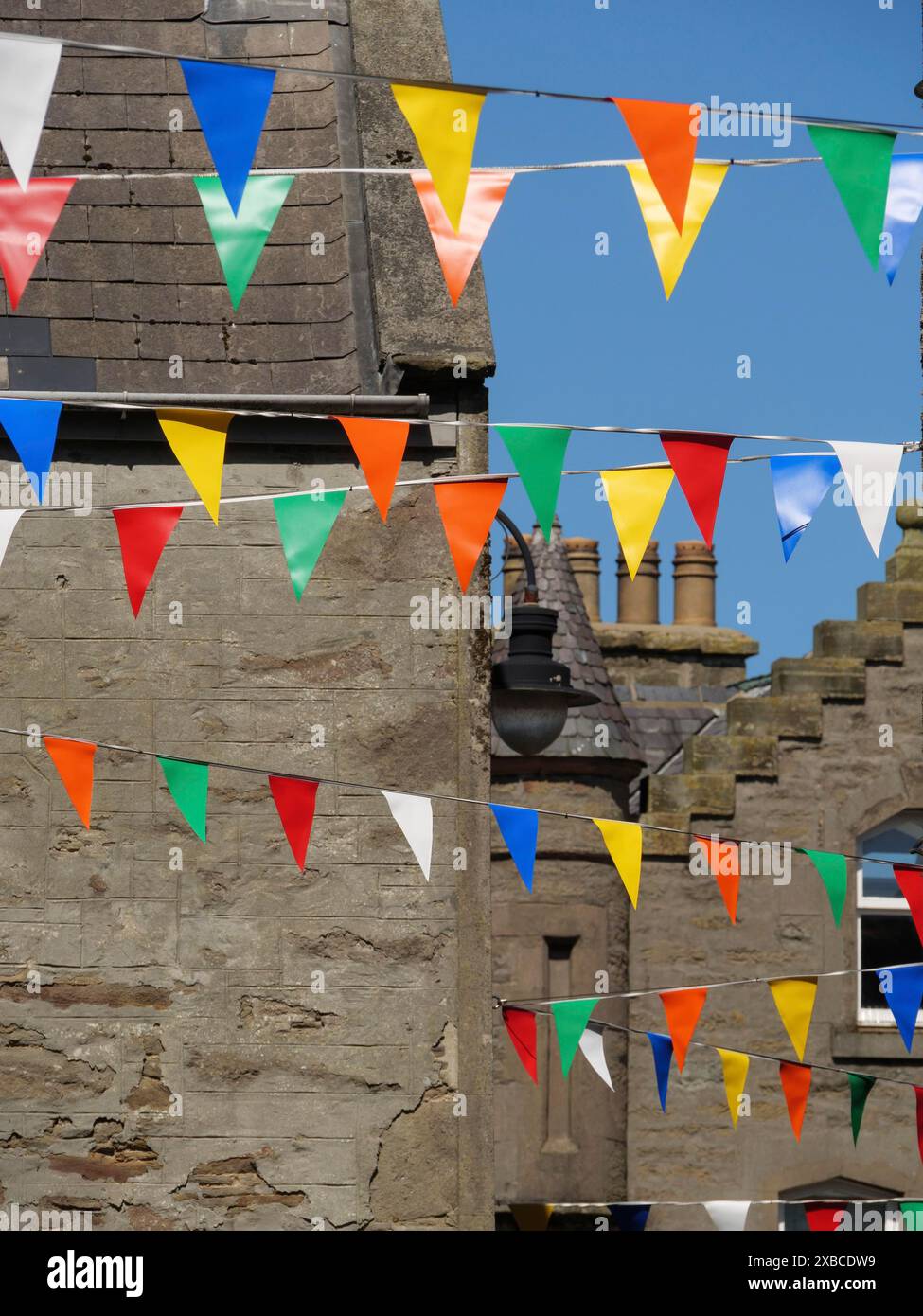 Colourful flags hang between traditional buildings under a bright sky ...