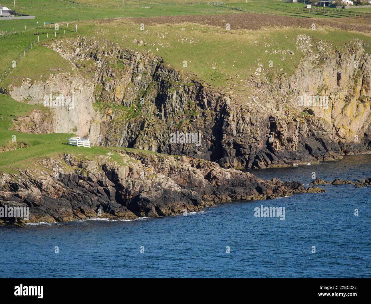 Rugged coastal cliffs of rocks with green hills and sea views under a ...