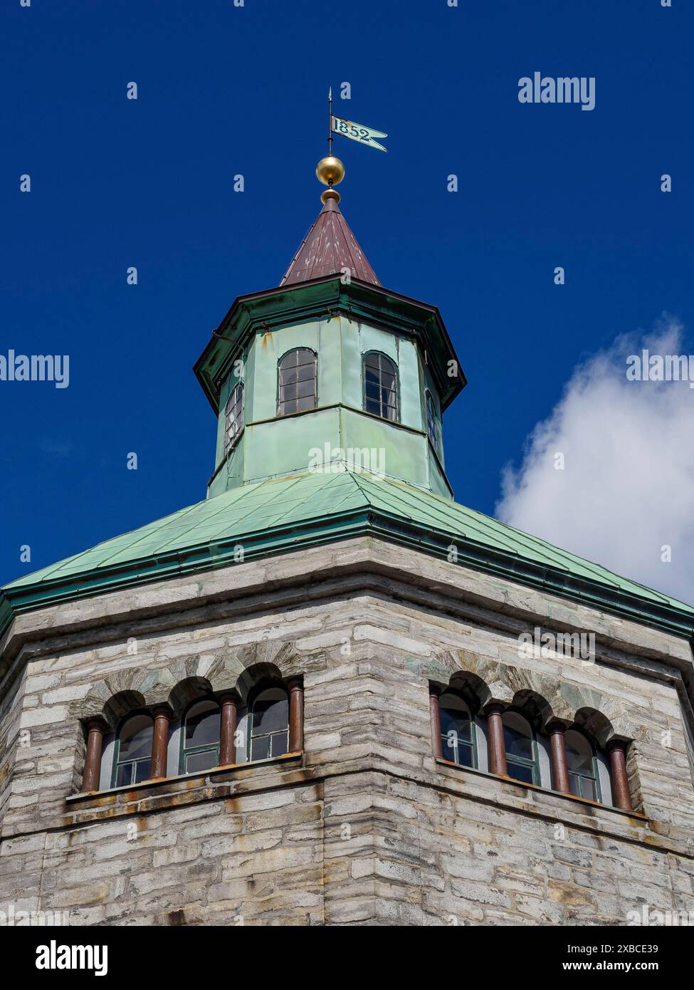 An old stone tower with a green roof and weather vane under a clear ...
