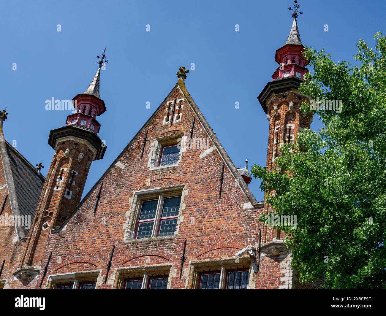 Historic brick building with pointed gables and towers next to a tree ...