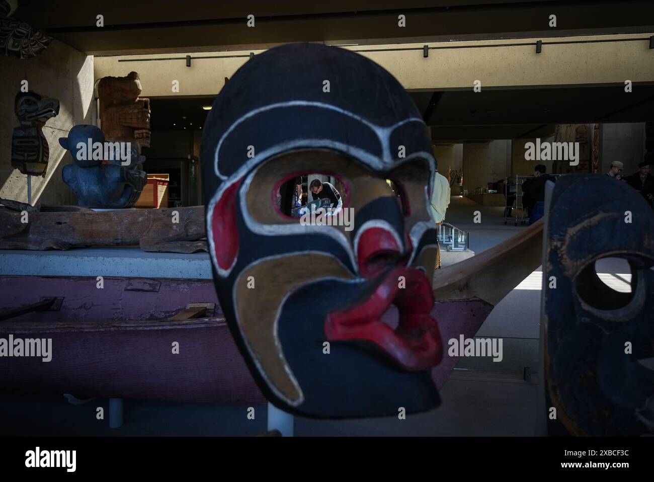 Framed by a First Nations mask, an employee moves an artifact as ...