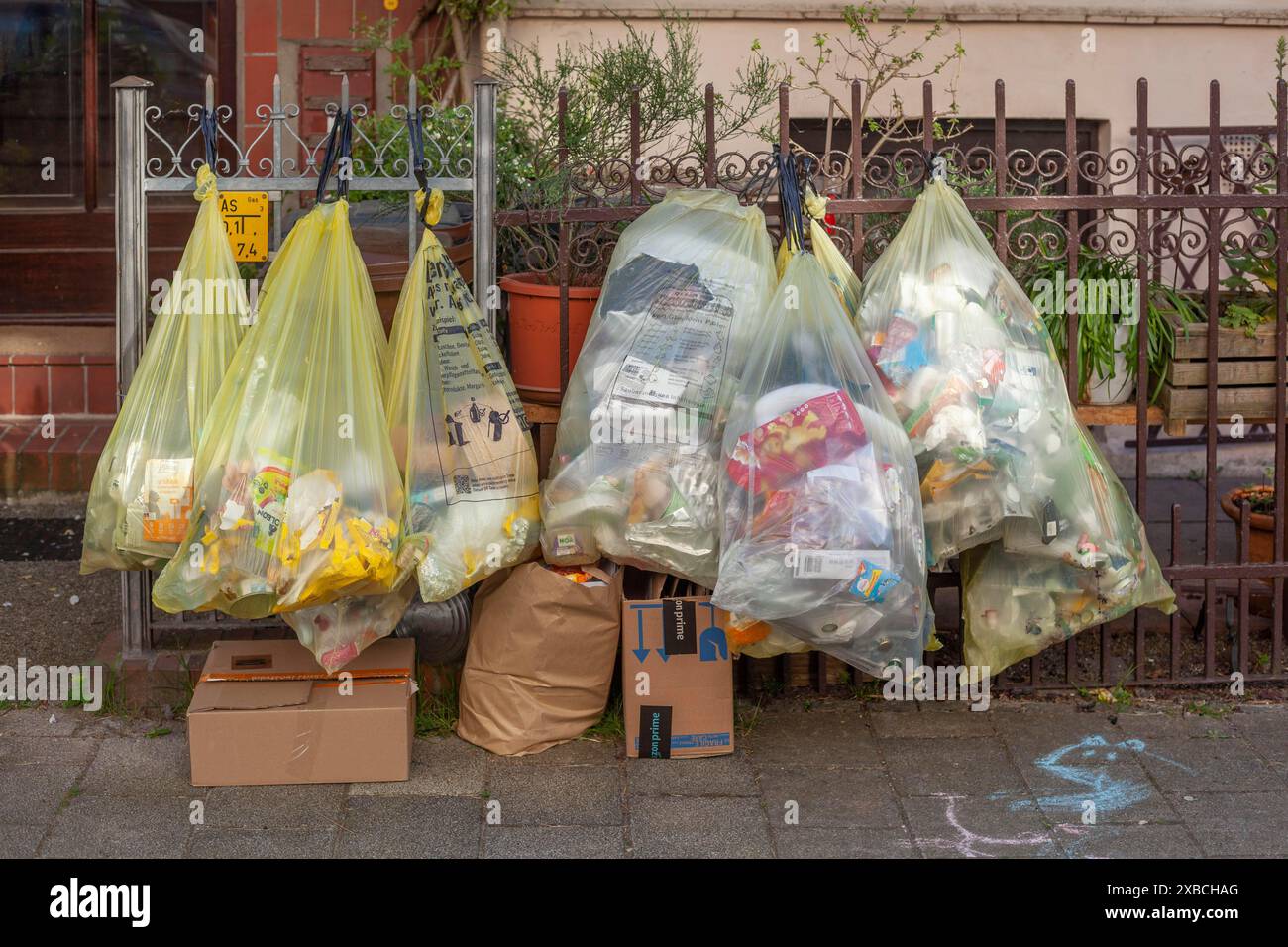 Yellow bags for plastic waste, hanging on a garden fence in front of a ...