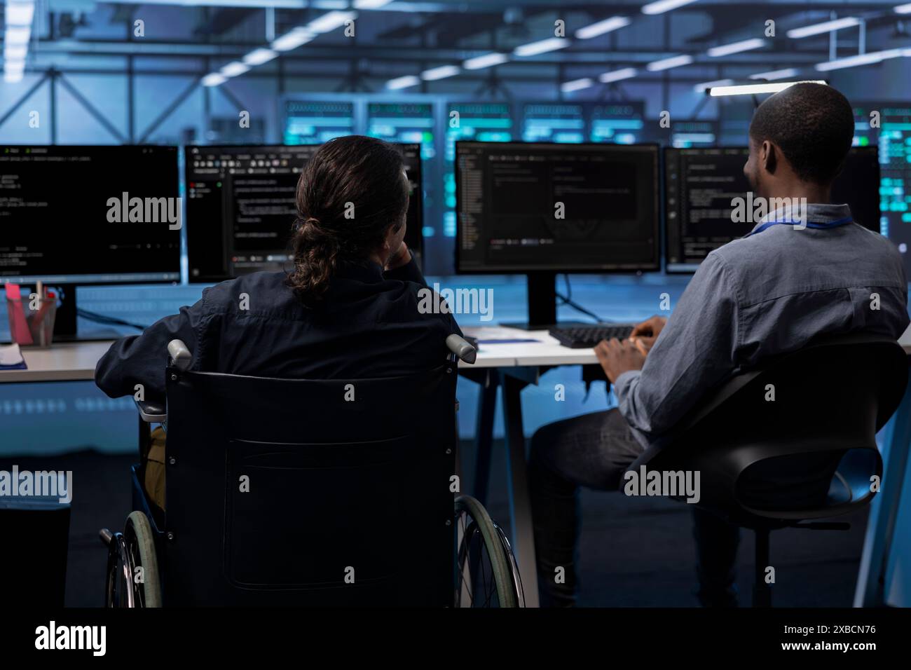 Person with paraplegia and colleague working in inclusive server hub workspace, typing on PC ...
