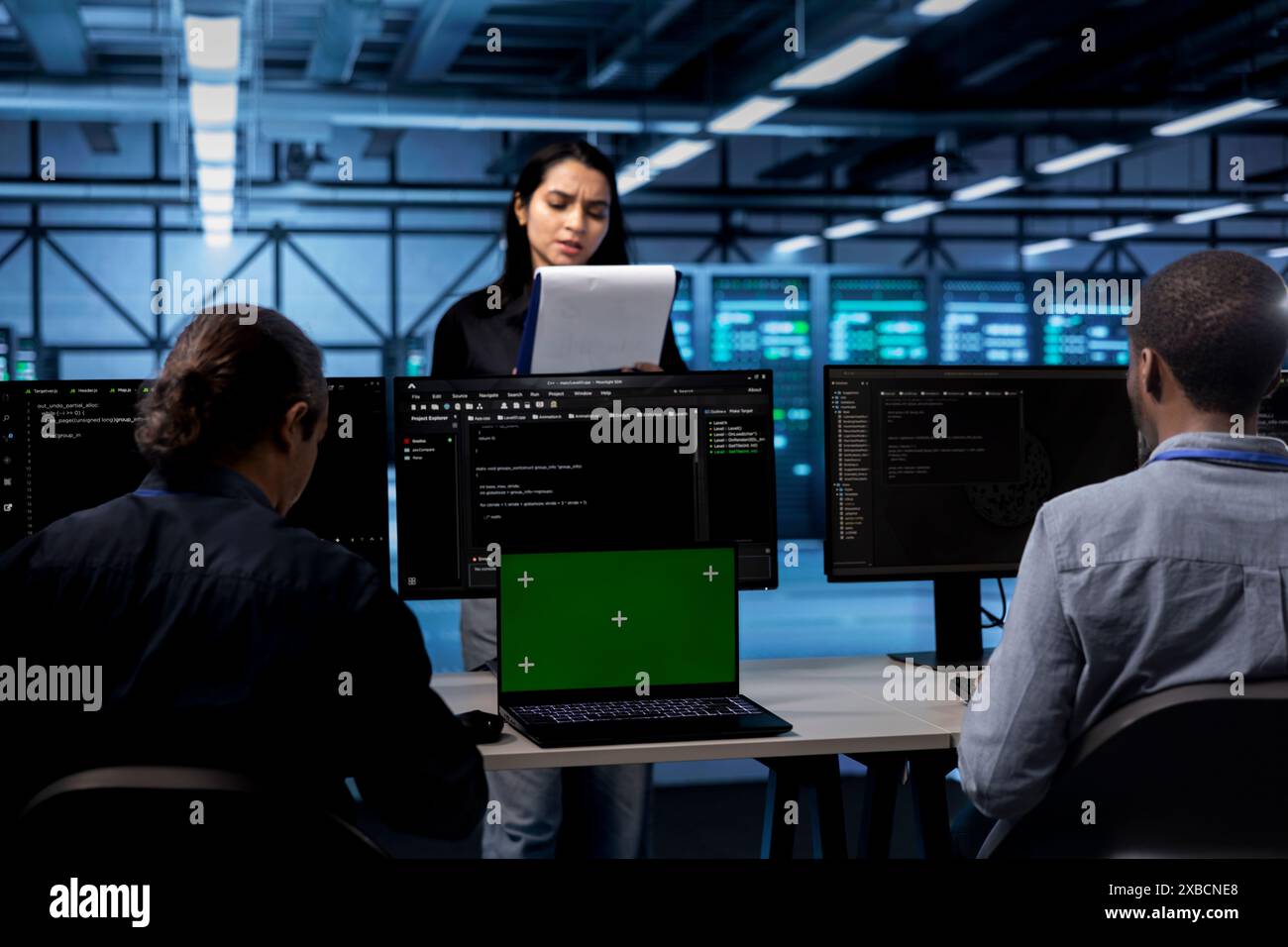 Manager inspecting server room equipment, reading paperwork from folder while engineers work on ...