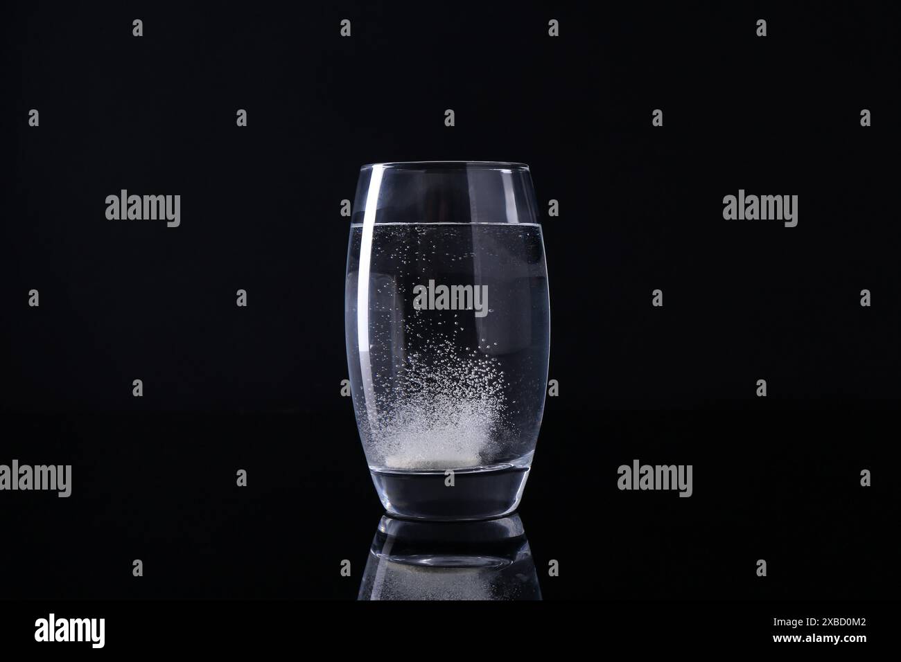 Effervescent pill dissolving in glass of water on black background ...