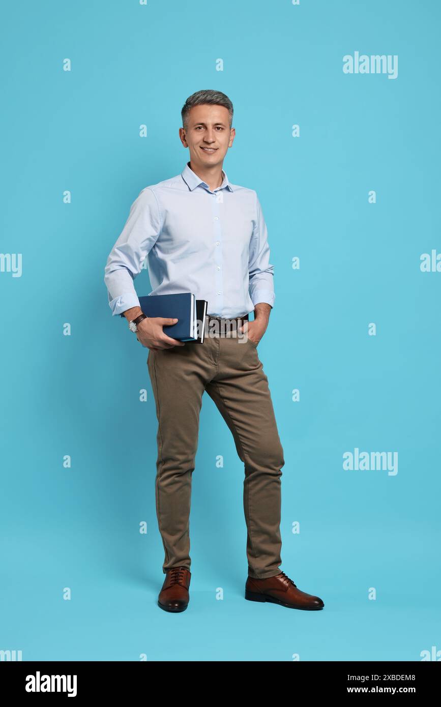 Teacher with books on light blue background Stock Photo - Alamy