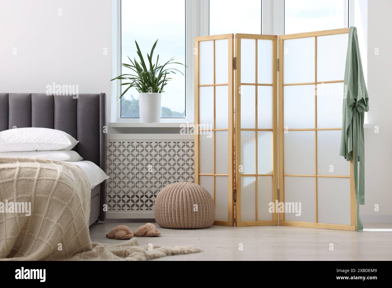 Folding screen, pouffe, bed and houseplant in bedroom Stock Photo - Alamy