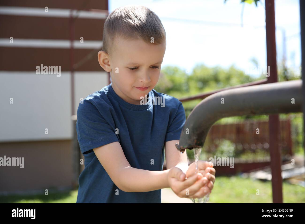 Water scarcity. Cute little boy drawing water with hands from tap ...