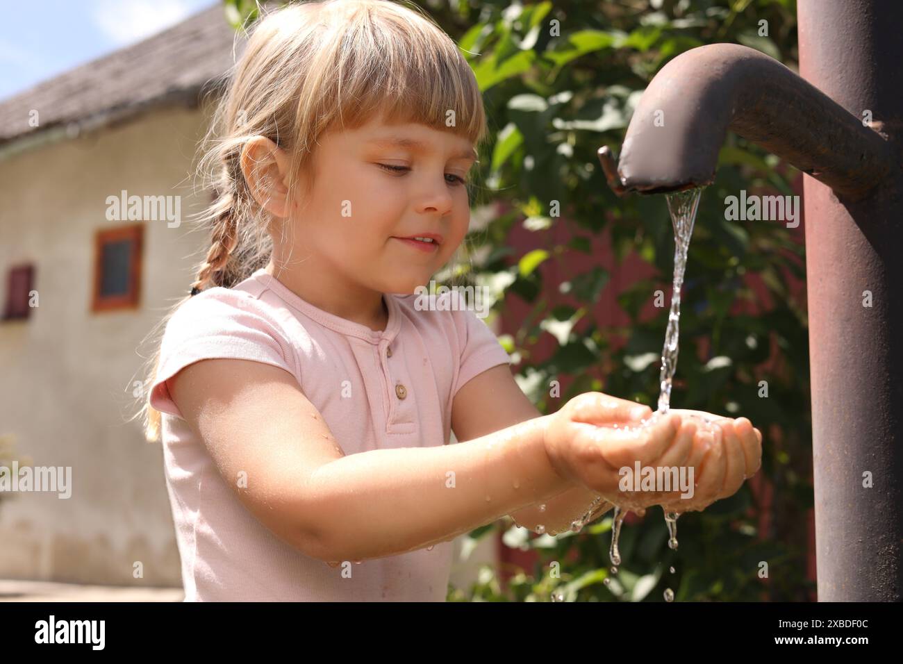 Water scarcity. Cute little girl drawing water with hands from tap ...