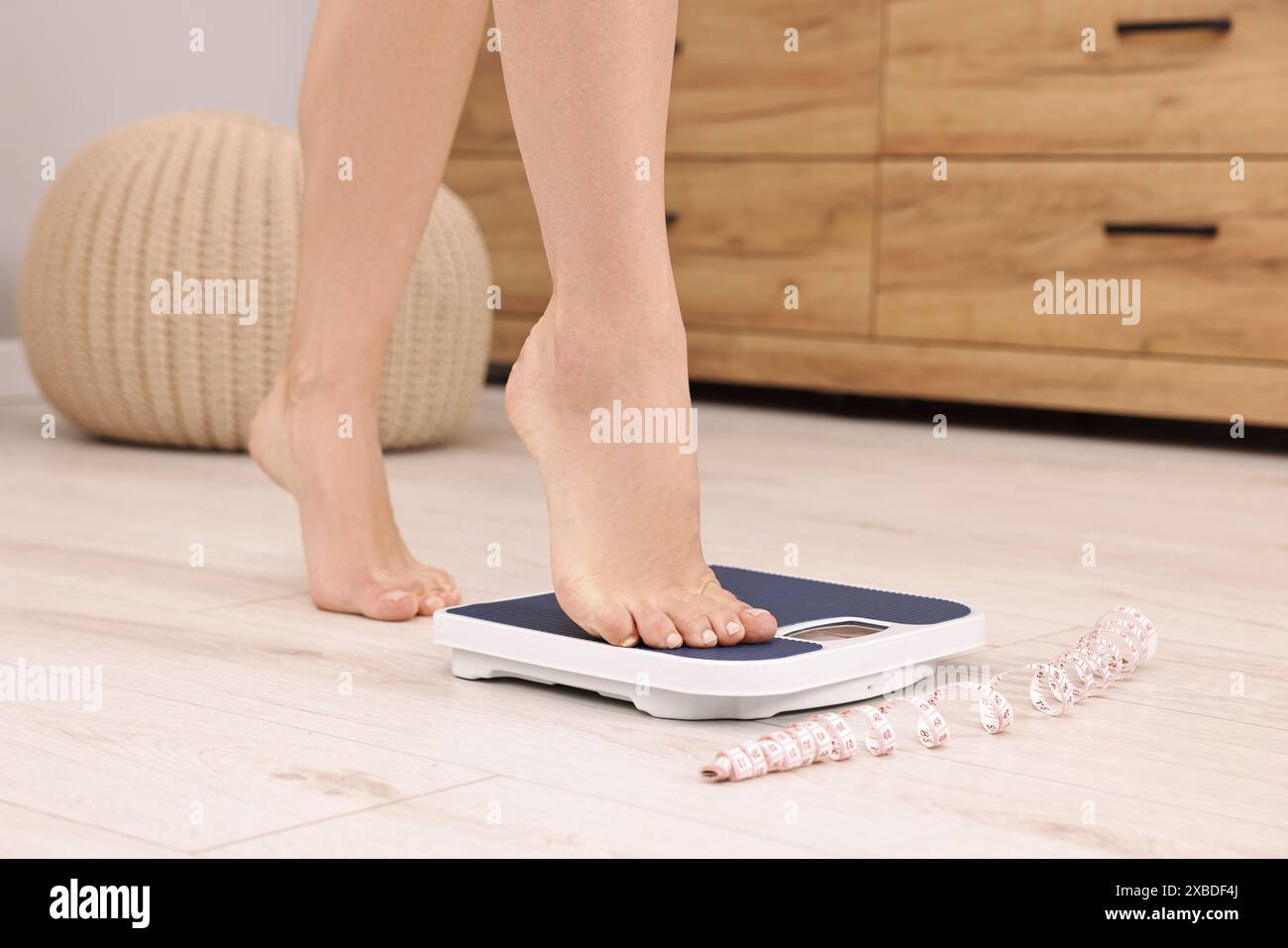 Woman stepping on floor scale and measuring tape at home, closeup ...