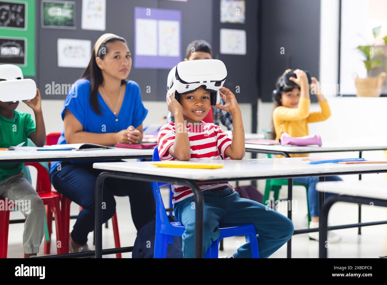 Biracial female teacher and children using VR sets in classroom Stock ...