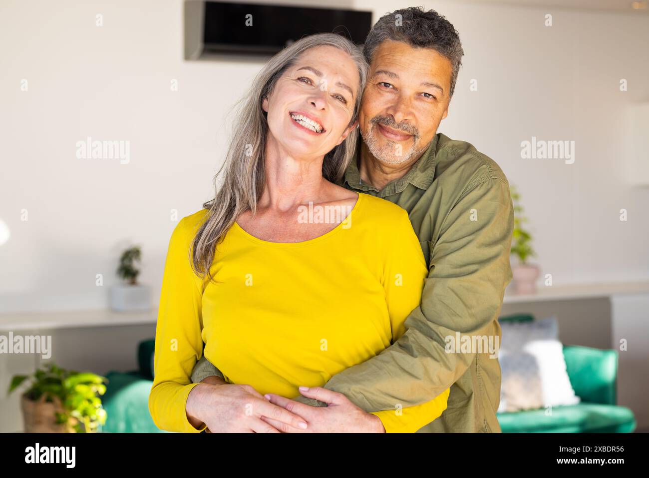 A biracial mature couple is smiling warmly while embracing each other ...