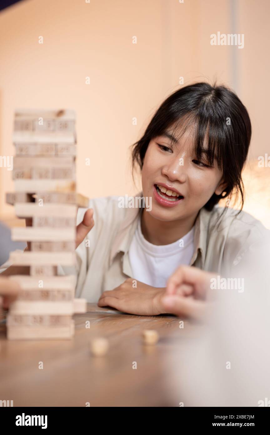 A young, cheerful Asian girl is enjoying playing Jenga with her friends ...