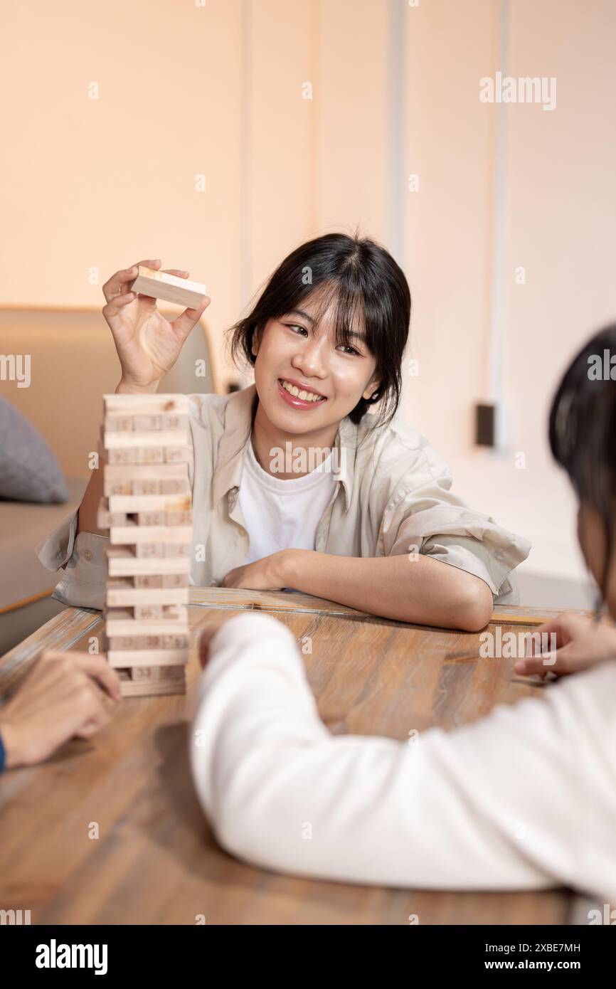 A young, cheerful Asian girl is enjoying playing Jenga with her friends ...