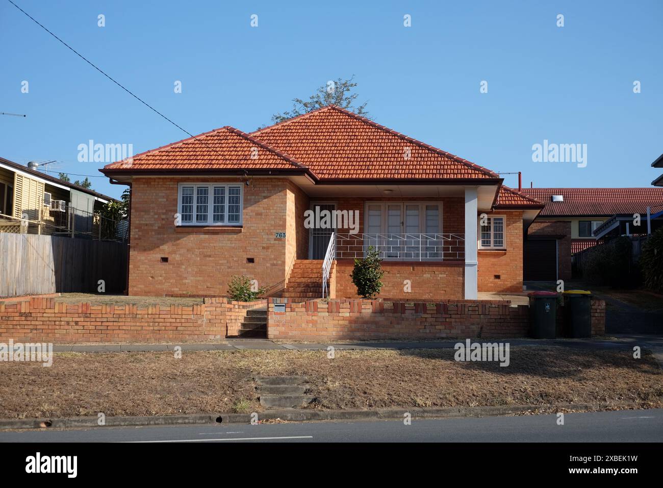 A boxy brick house with red tiled roof, matching brick front fence ...