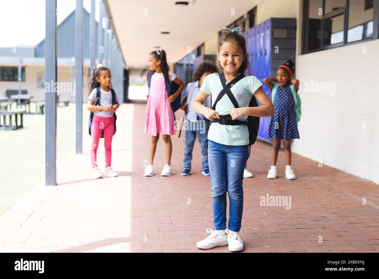 Biracial students standing outside school building, wearing backpacks ...