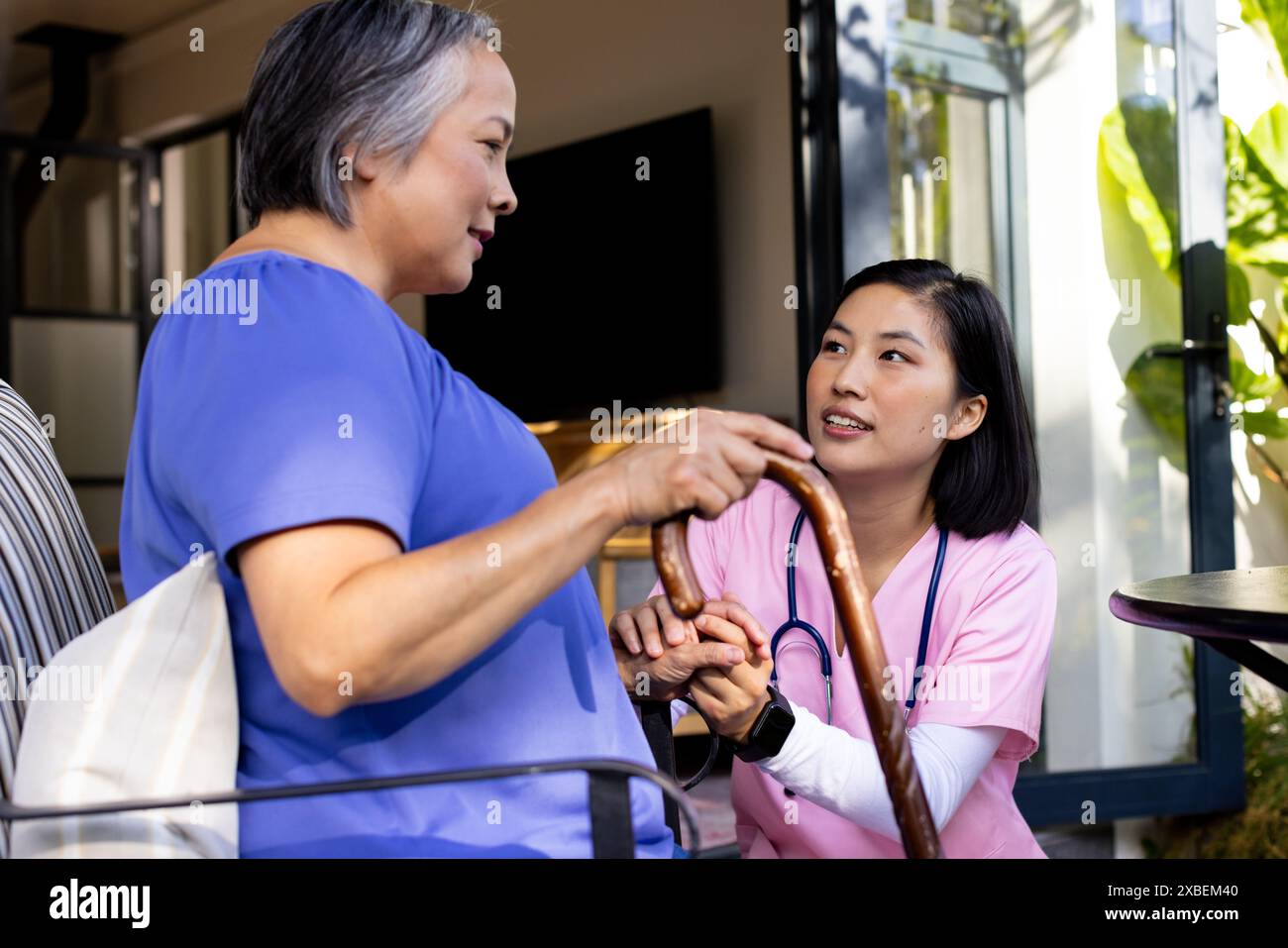 Asian senior woman with cane assisted by young Asian woman in scrubs ...