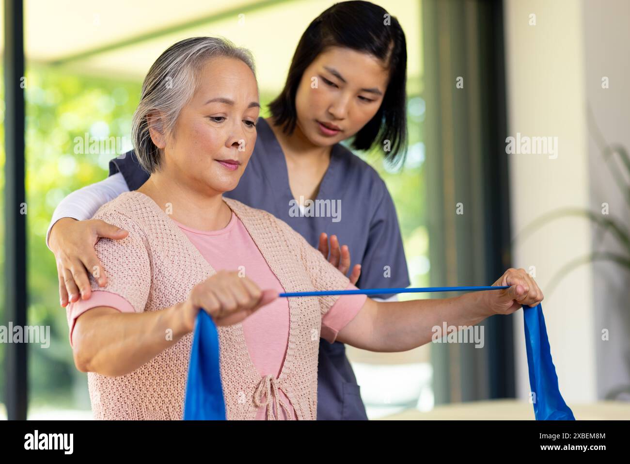 Asian senior woman exercises with resistance band, aided by Asian ...