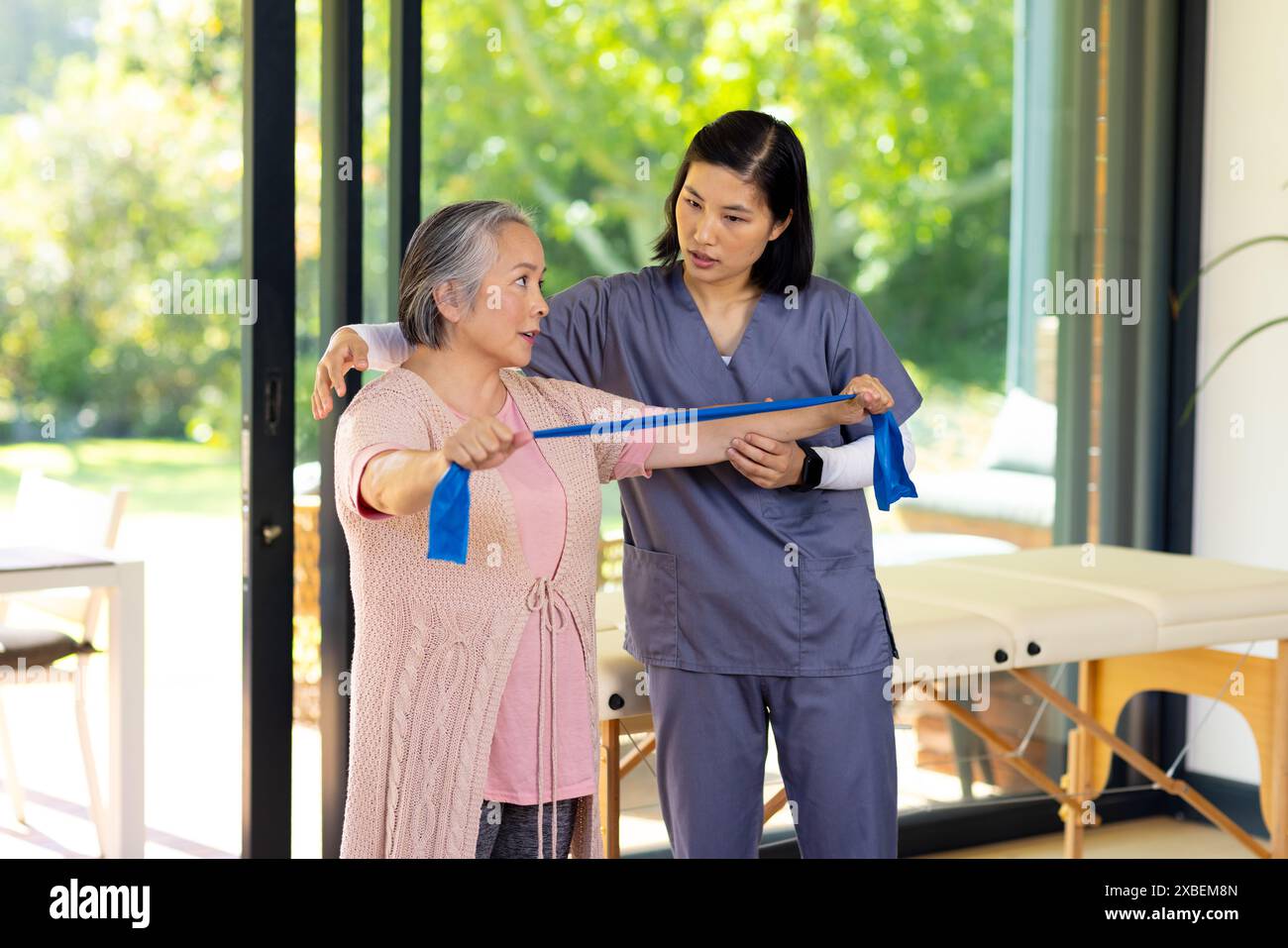Physical therapist helps senior Asian woman with resistance band ...