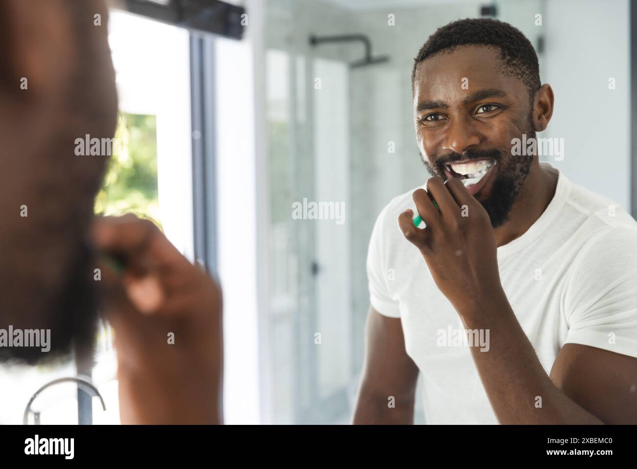 African American young man brushing teeth in bathroom mirror, smiling and focused, at home Stock ...