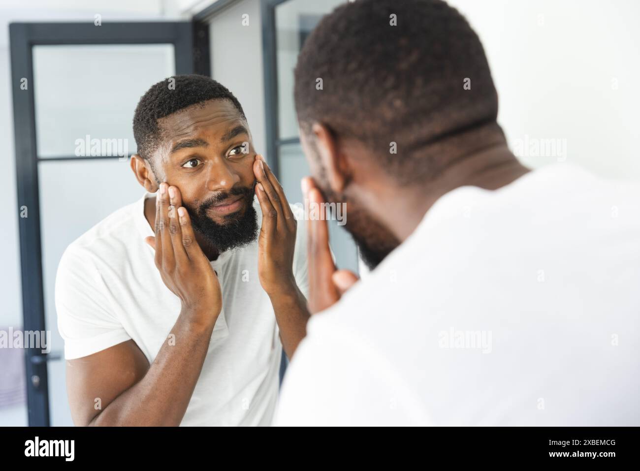 African American young man grooming in front of mirror, touching his ...
