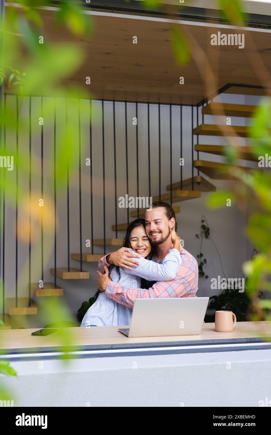 Young diverse couple hug while seated at a table with a laptop Stock ...